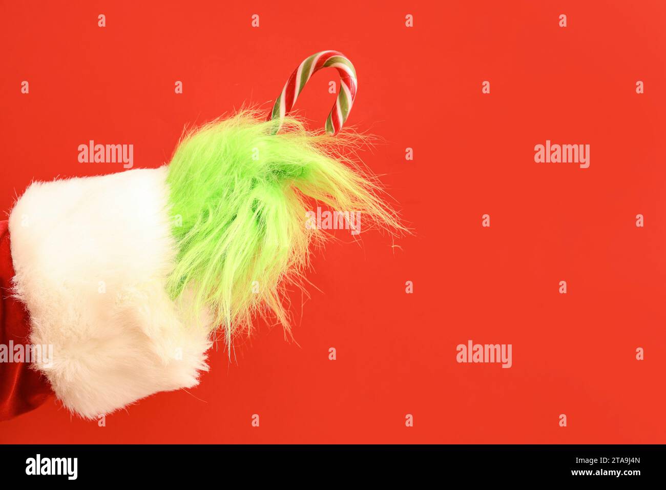 Green hairy hand of creature in Santa costume with candy cane on red ...