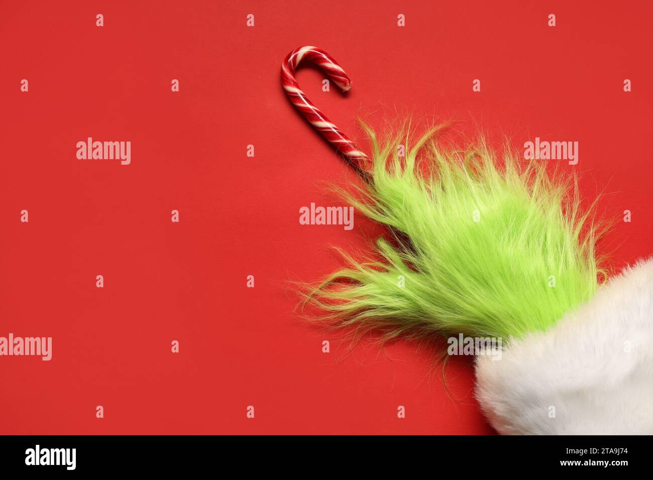 Green hairy hand of creature in Santa costume with candy cane on red ...