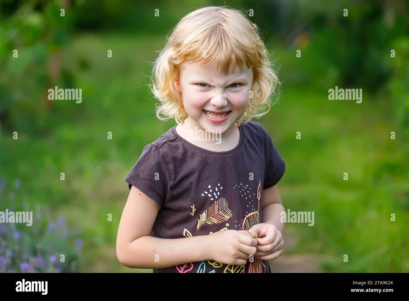 Angry little girl writhing her face in the park on the background of ...