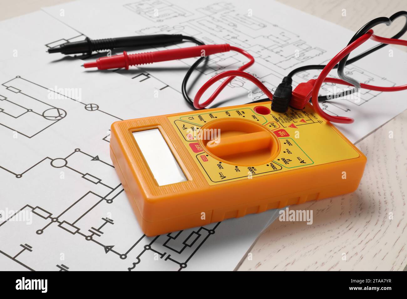 Wiring diagrams and digital multimeter on white wooden table, closeup ...