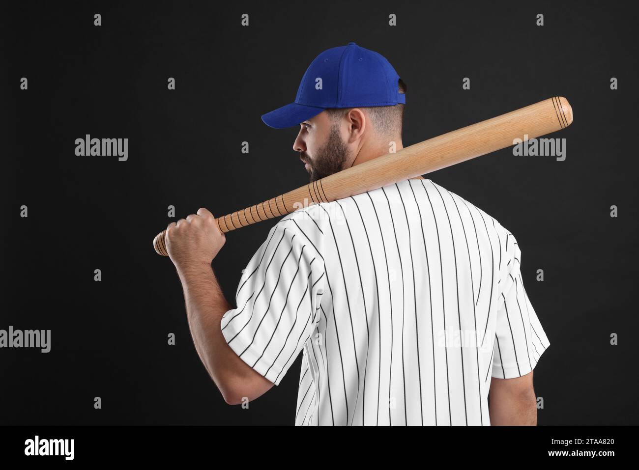 Man in stylish blue baseball cap holding bat on black background, back ...
