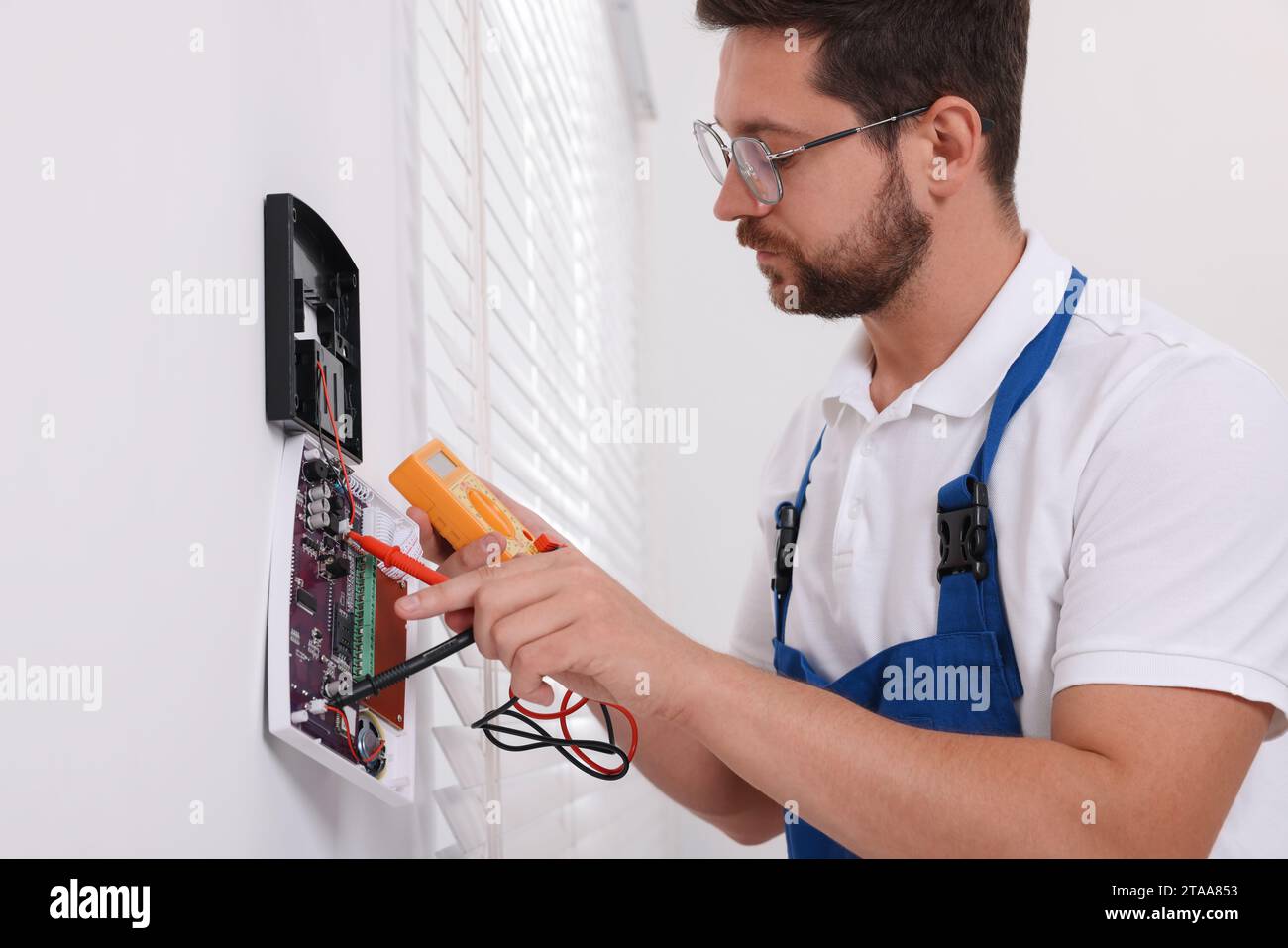 Technician using digital multimeter while installing home security ...