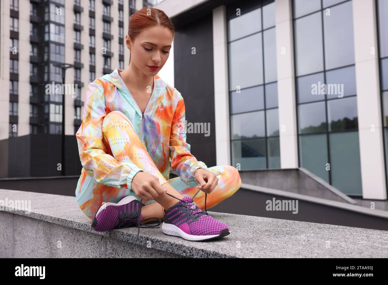 Woman sitting on parapet and tying shoelace of sneakers on street ...
