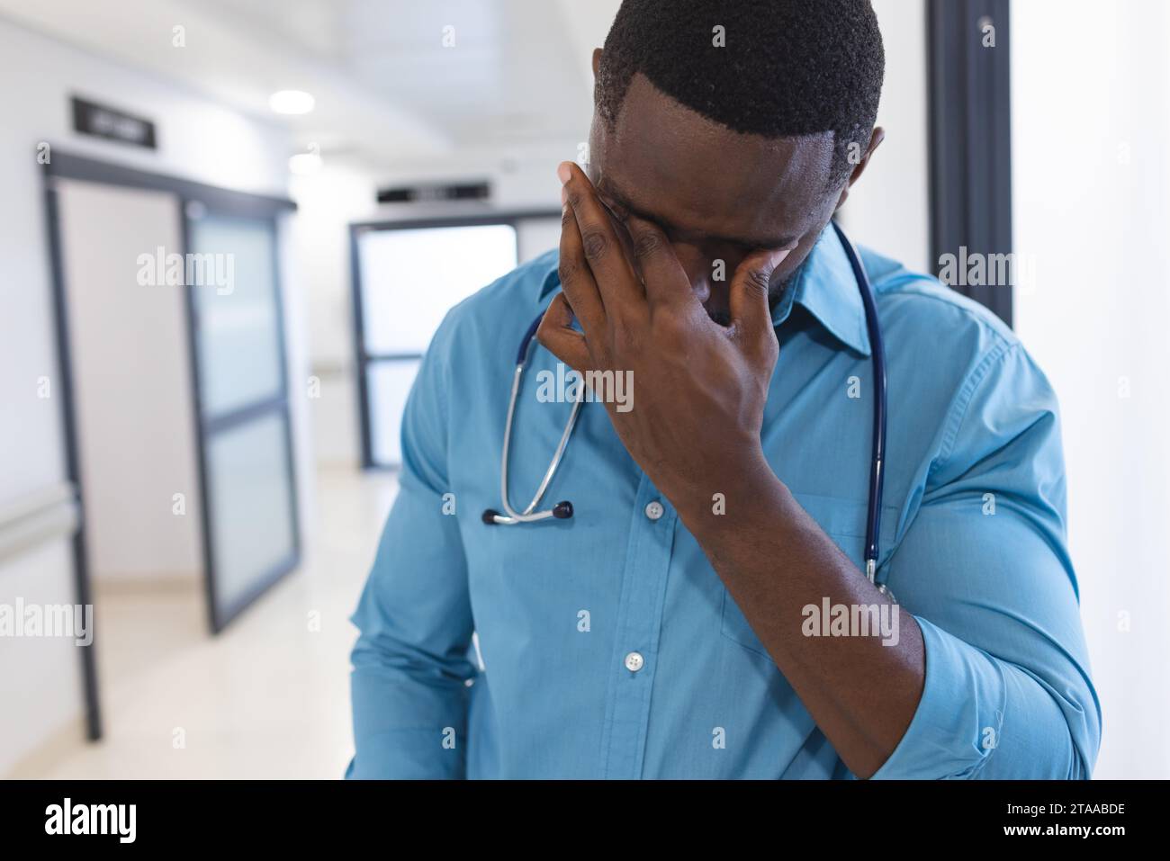 Sad african american male doctor wearing blue shirt in corridor in ...