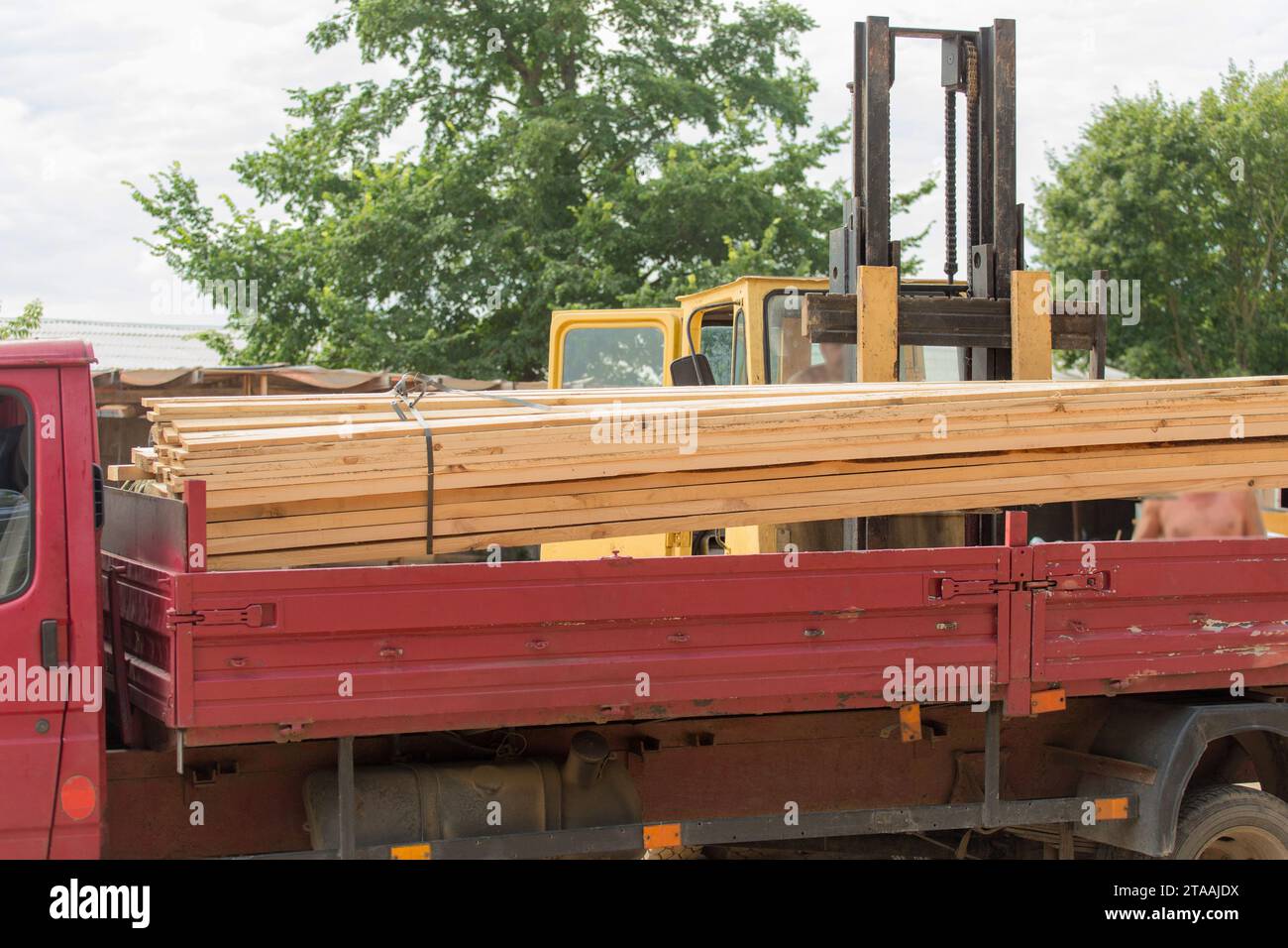 A forklift loads wooden planks into the back of a trailer car. Wood ...
