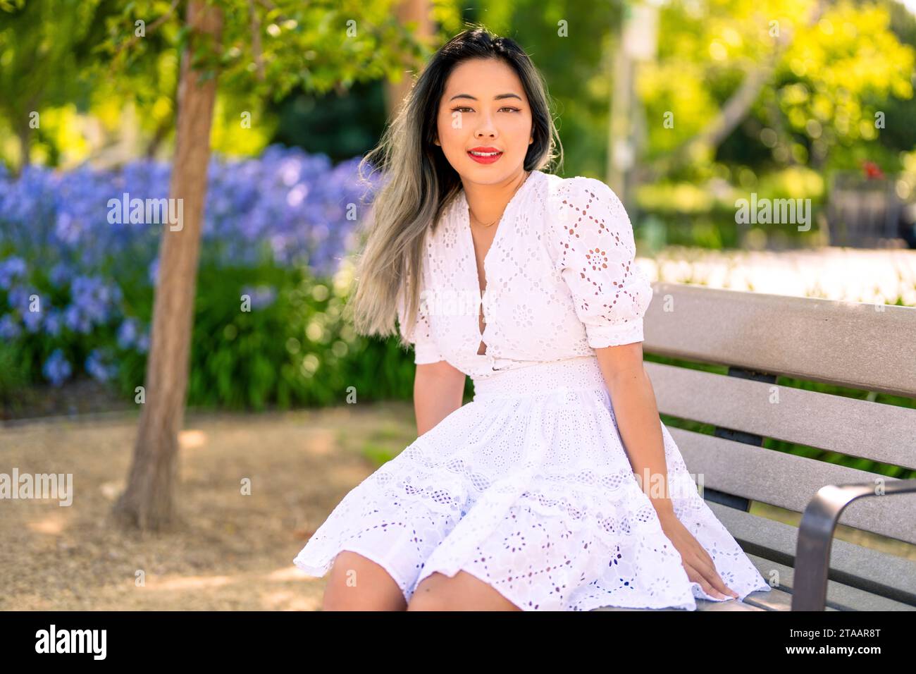 Young Asian Woman Sitting on a Park Bench Surrounded by Colorful Plants ...