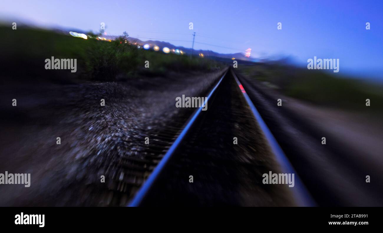 Dreamy vision of parallel train-tracks that absorb the darkness of twilight to converge and ...