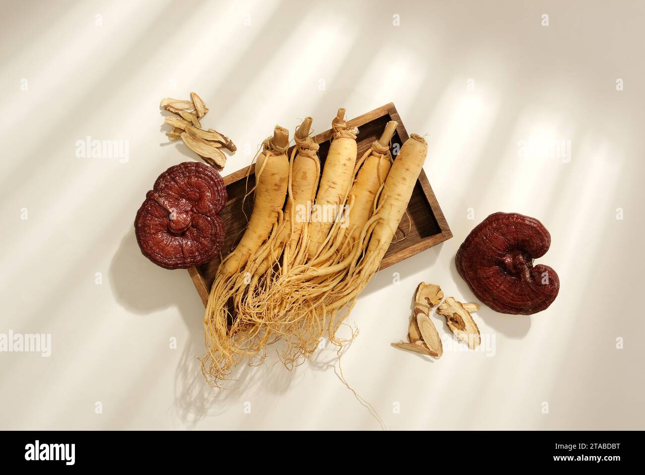 On a white background with shadow of window, a wooden tray of ginseng ...