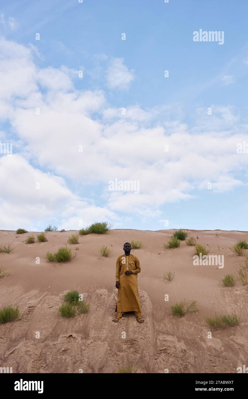 Vertical wide angle shot of Black man standing on sand dune in desert ...