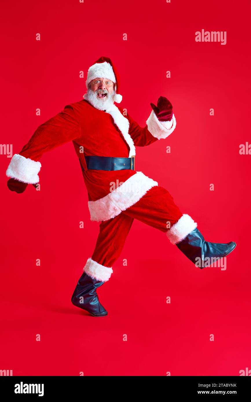 Cheerful man with grey hair waring Santa Claus costume jumps merrily ...