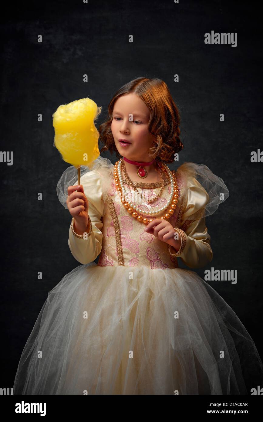 Little princess in old-fashioned dress eating, tasting bright yellow ...