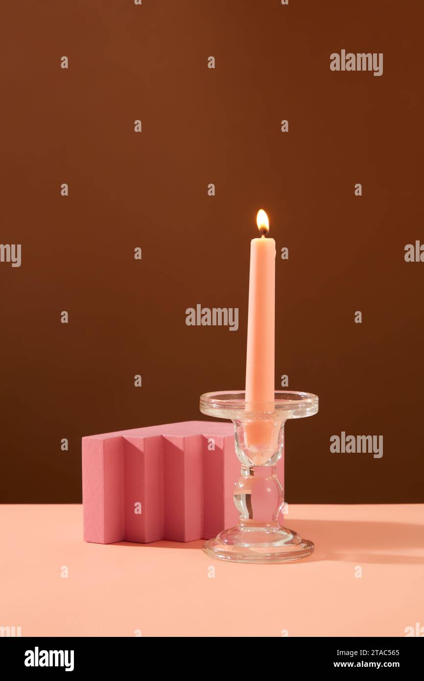 Front view of a burning pink candle is placed on a glass candlestick ...
