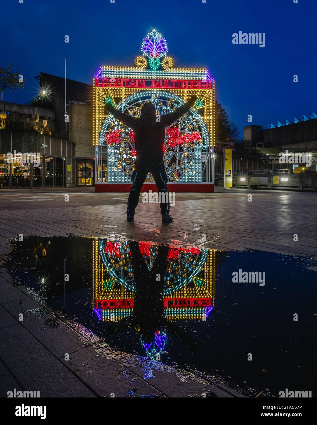 A man raises his arms in victory by the reflection of We Rise By ...