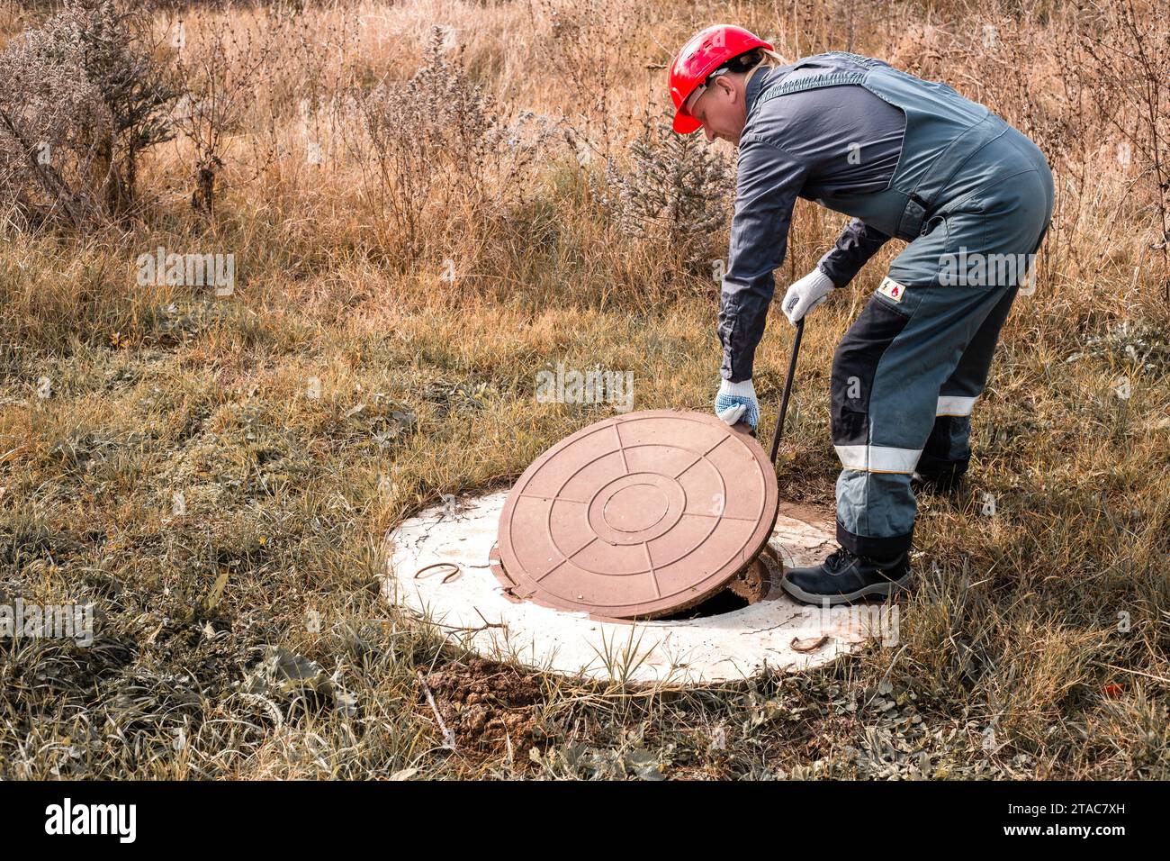 A worker in a hard hat lifts a manhole cover on a septic well ...