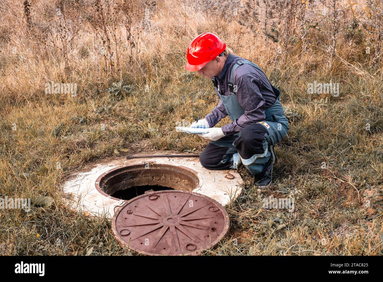 A utility worker in a helmet records the readings of a water meter in a ...