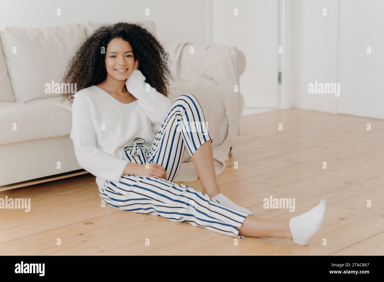 Relaxed Black woman with curly hair sitting on the floor, smiling, home interior Stock Photo - Alamy