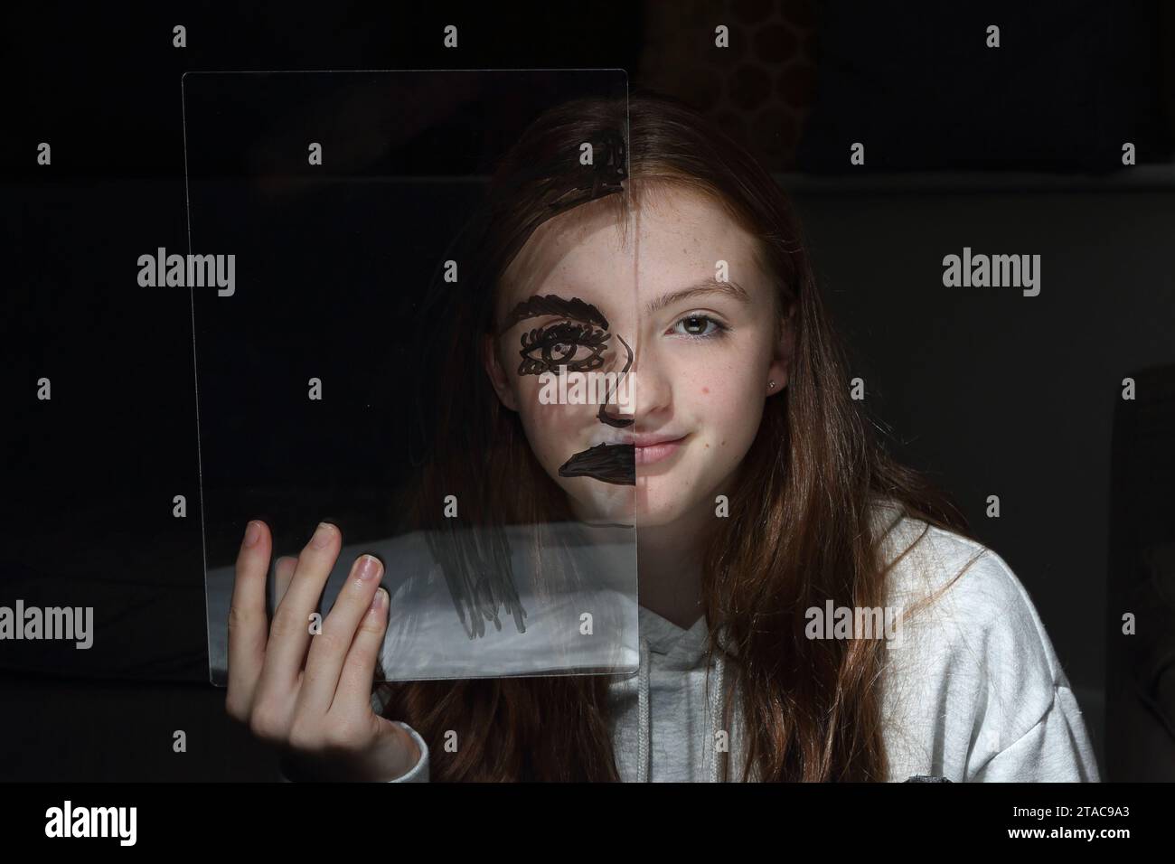 Teenage girl holds a tranparent perspex sheet with drawing of half a ...