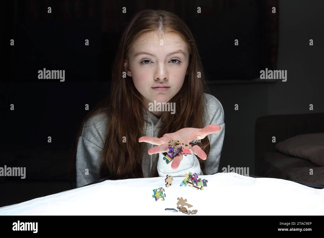 Teenage girl drops pieces of a jigsaw puzzle from her hand and they ...