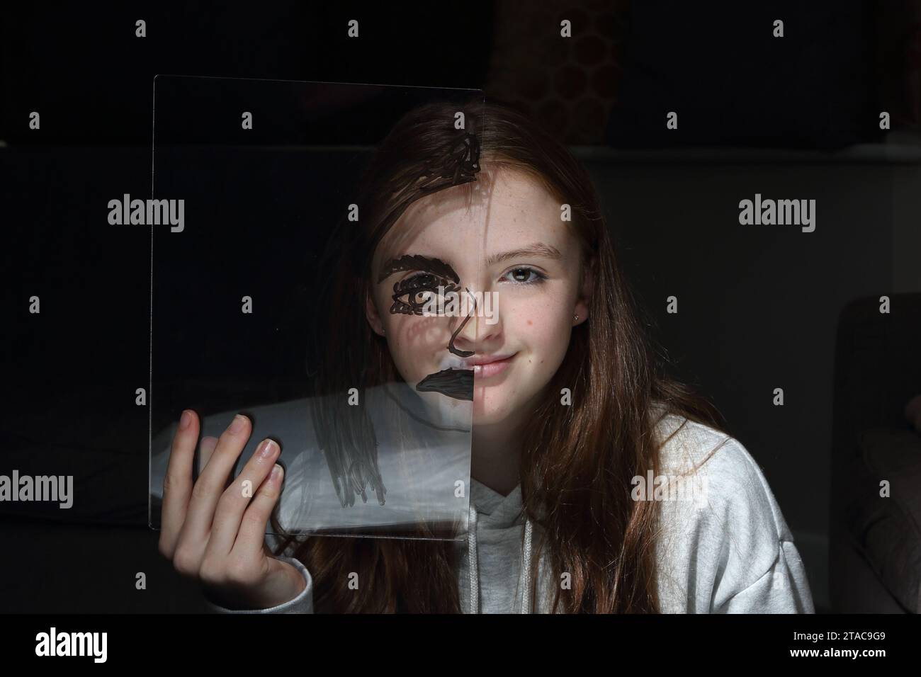 Teenage girl holds a tranparent perspex sheet with drawing of half a ...