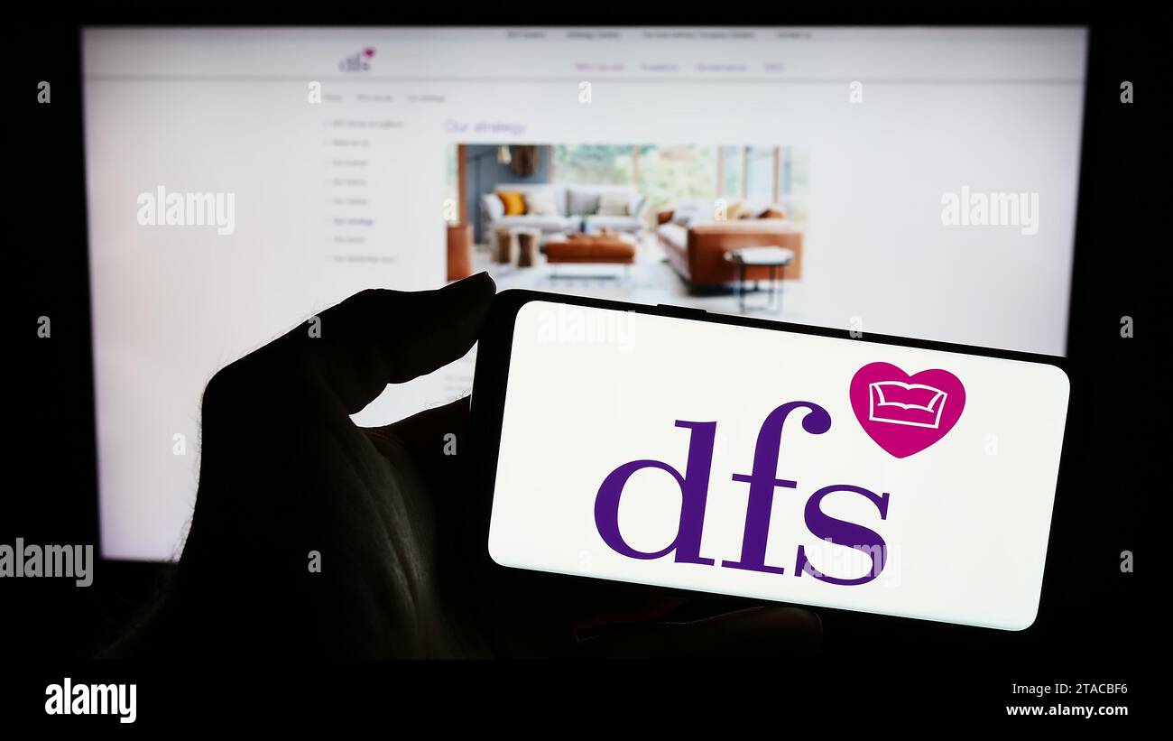 Person holding cellphone with logo of British retail company DFS Furniture plc in front of ...