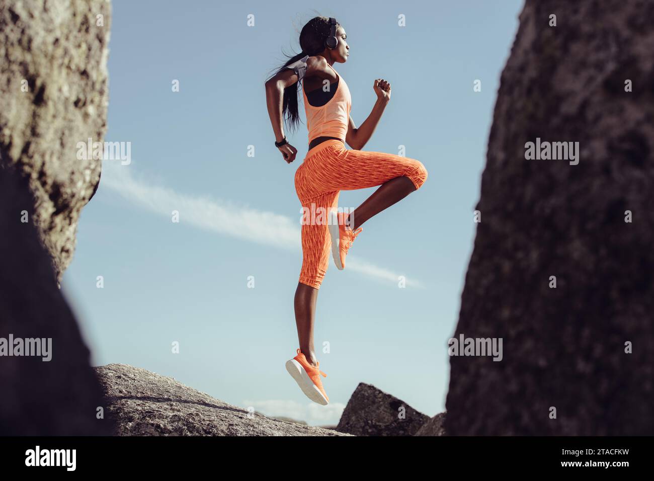 African female athlete jumping and stretching over rocks outdoors ...