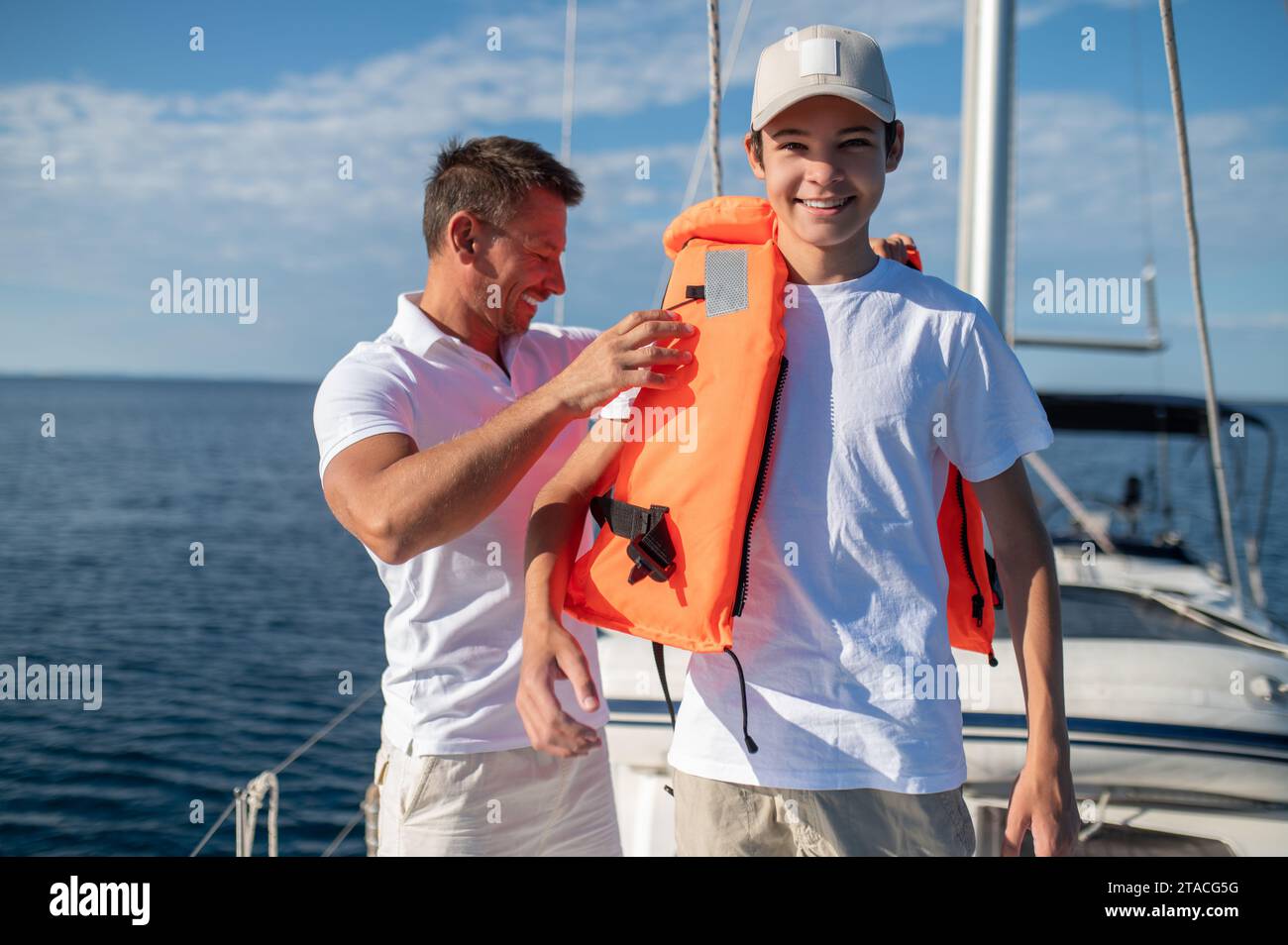 Father putting a life-jacket on his boy while sailing on the yacht ...