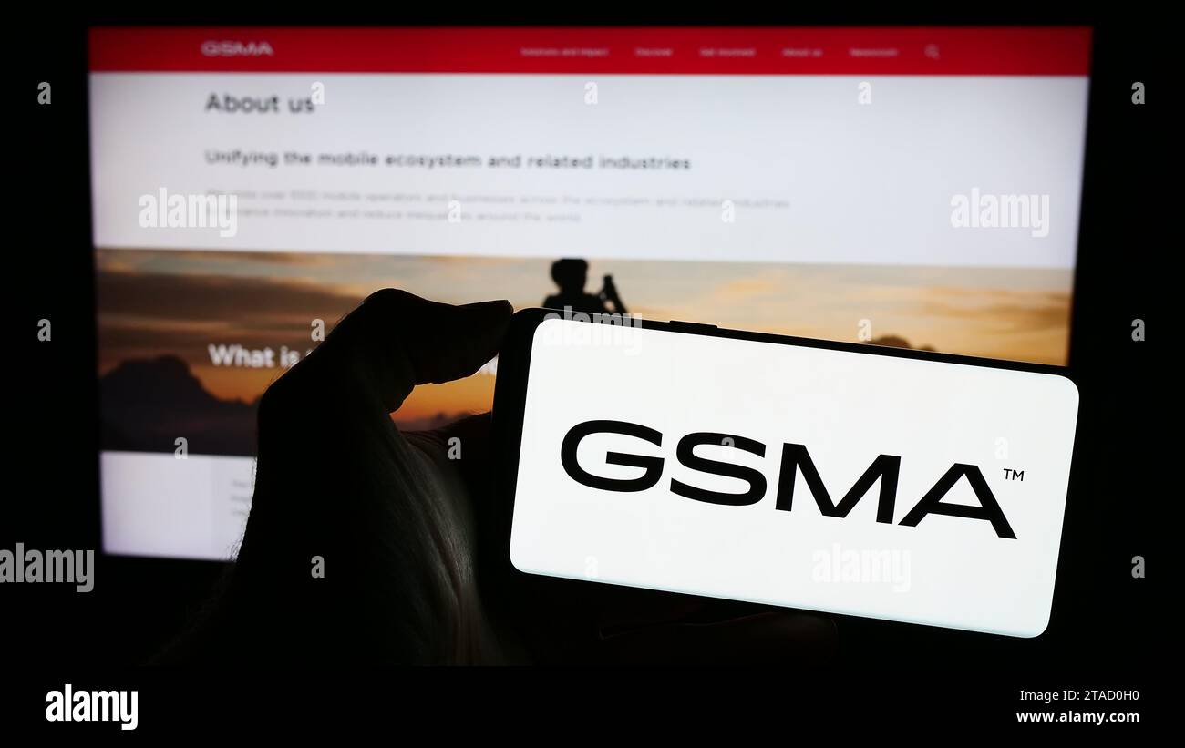 Person holding mobile phone with logo of mobile industry organisation GSM Association (GSMA) in ...