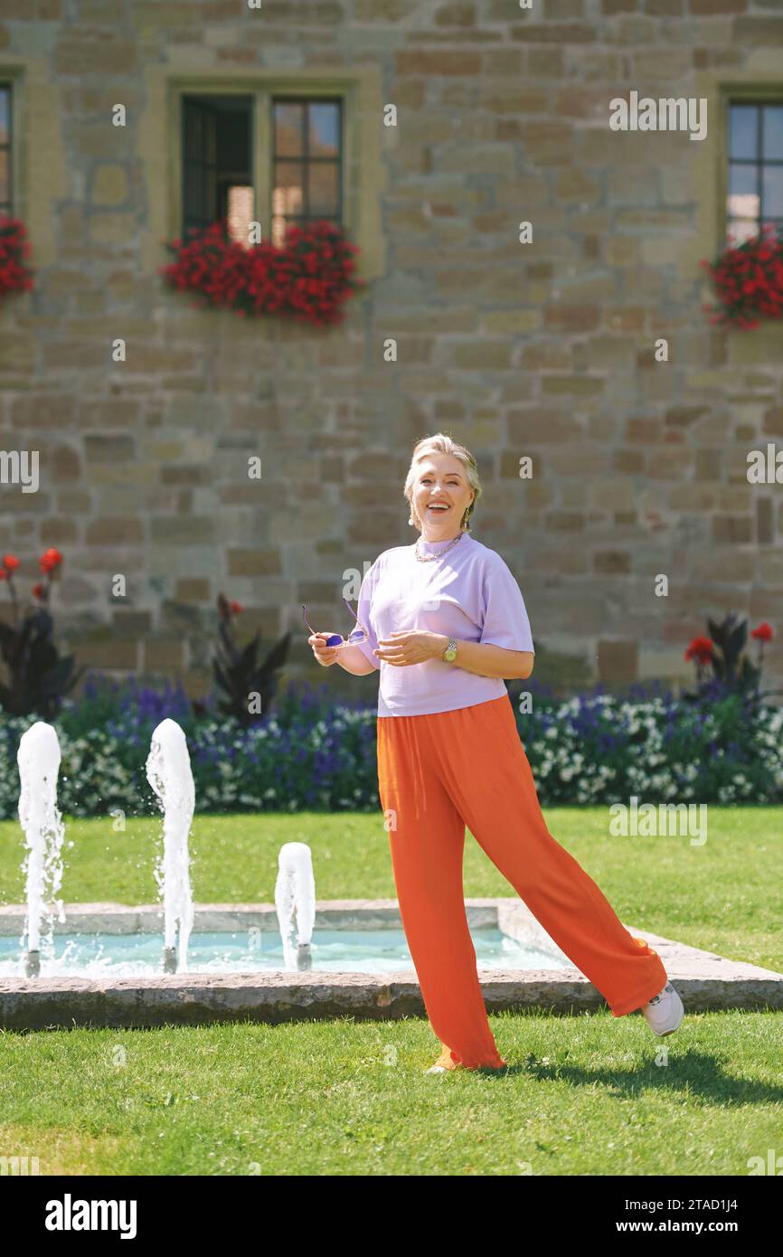 Outdoor portrait of beautiful and elegant middle age 55 - 60 year old woman, wearing bright ...