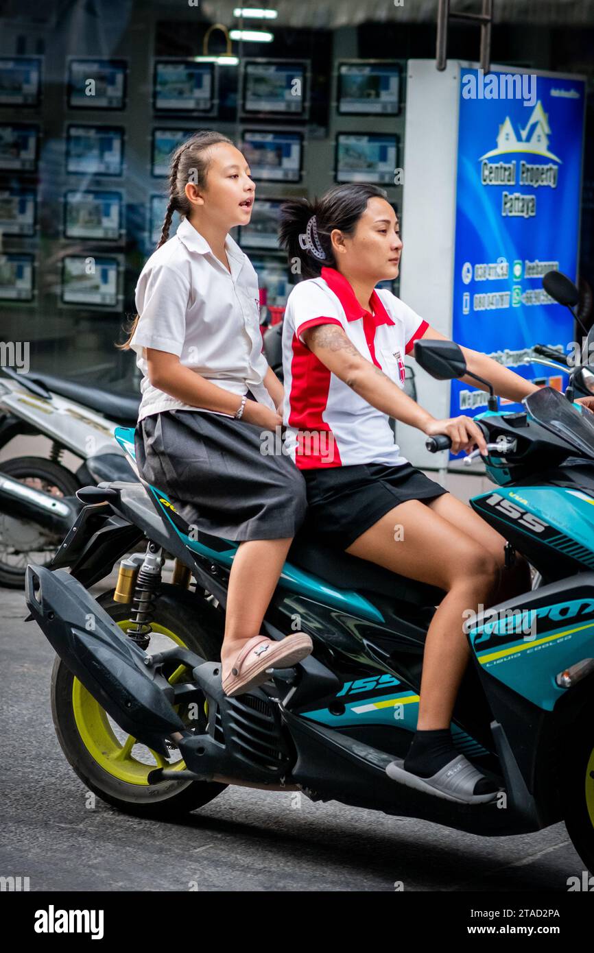 A Thai school girl sits at the back of a motorbike taxi travelling through the busy streets of ...