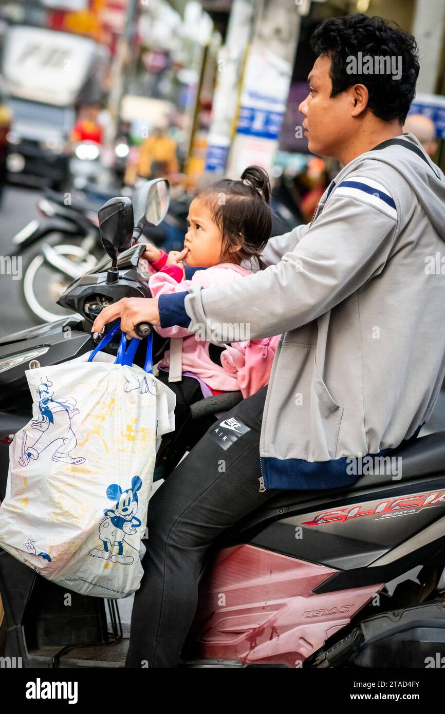 A young Thai girl gets a lift on the front of her dads moped through ...