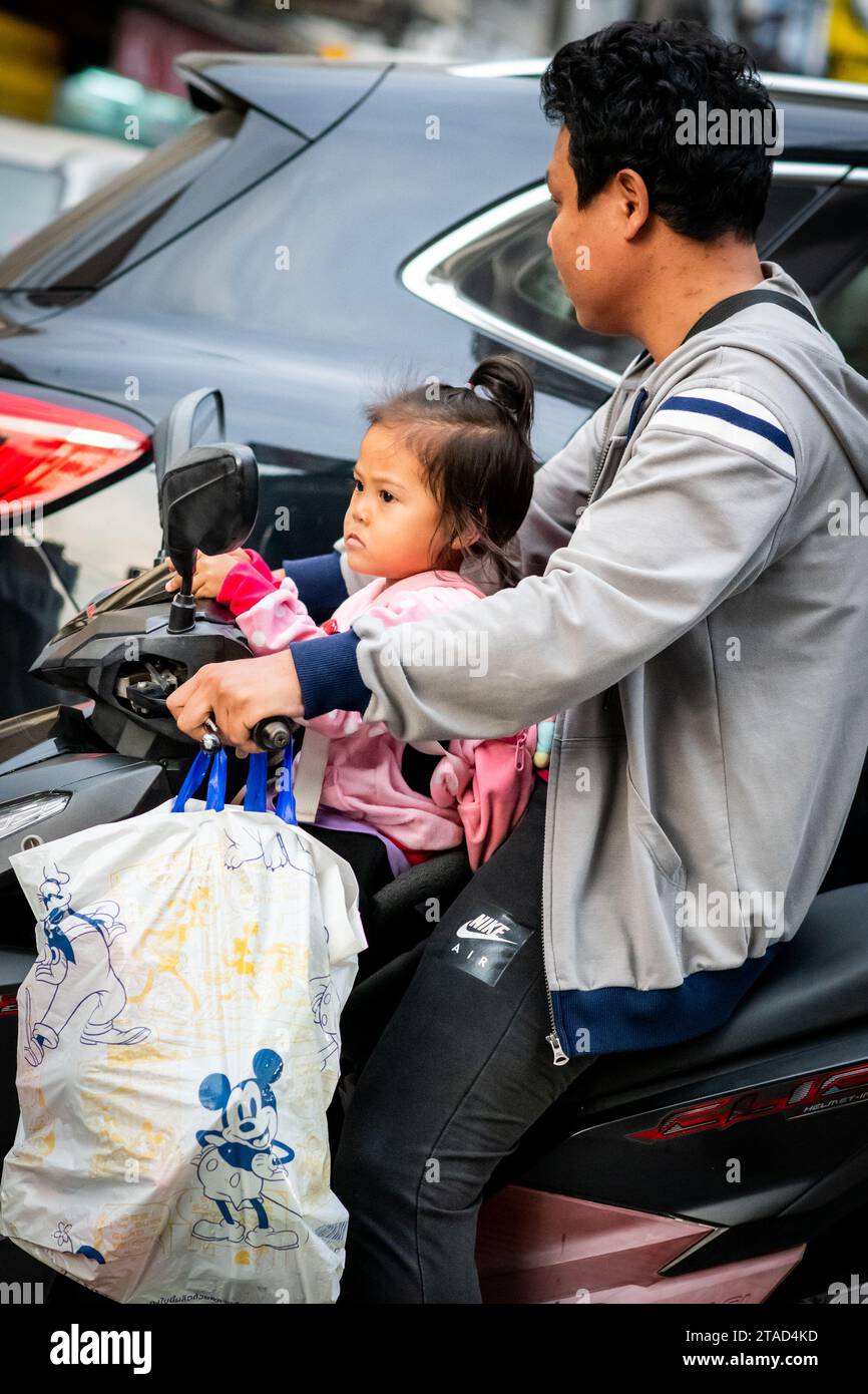 A young Thai girl gets a lift on the front of her dads moped through ...