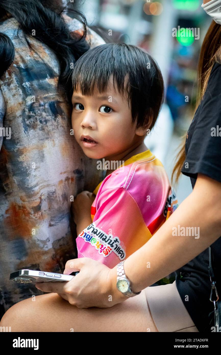 A little Thai boy is sat between two ladies, glances back at me on a motorbike travelling ...