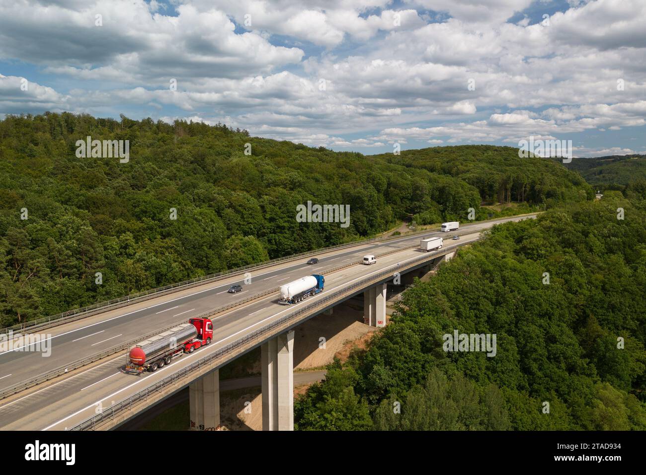 Multiple commercial trucks are travelling along a busy highway, passing ...