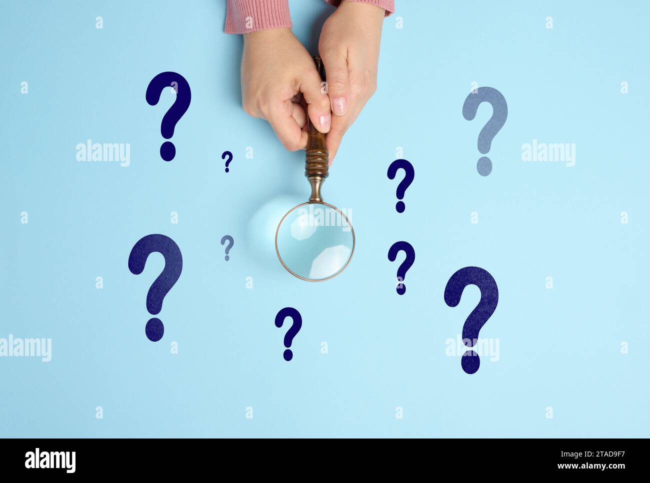 Female hand holds a wooden magnifying glass and question marks on a ...
