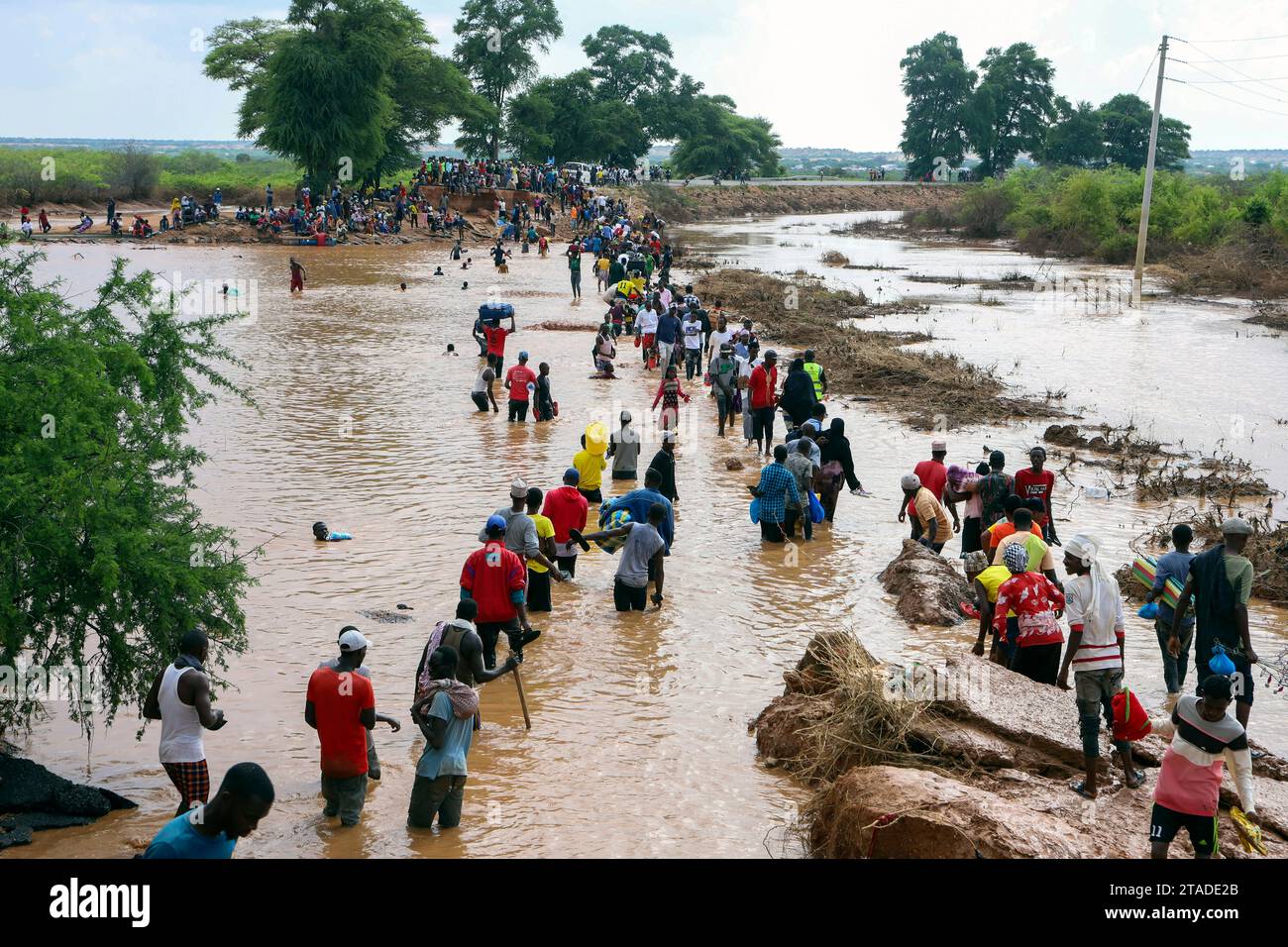 People wade over flood waters after a section of road was destroyed by ...
