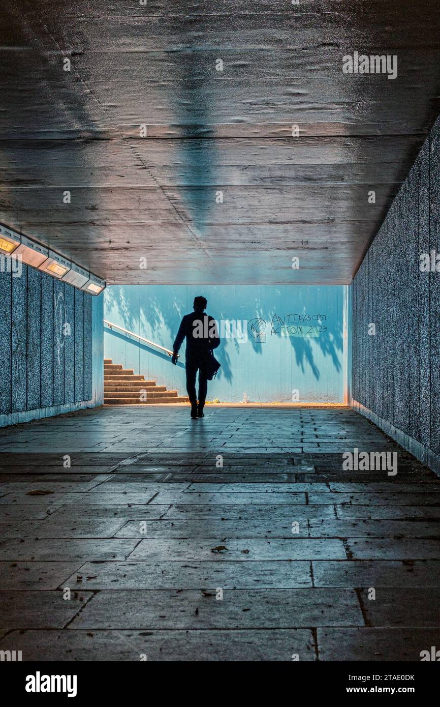 Silhouette of a person walking in a dark pedestrian underpass towards ...