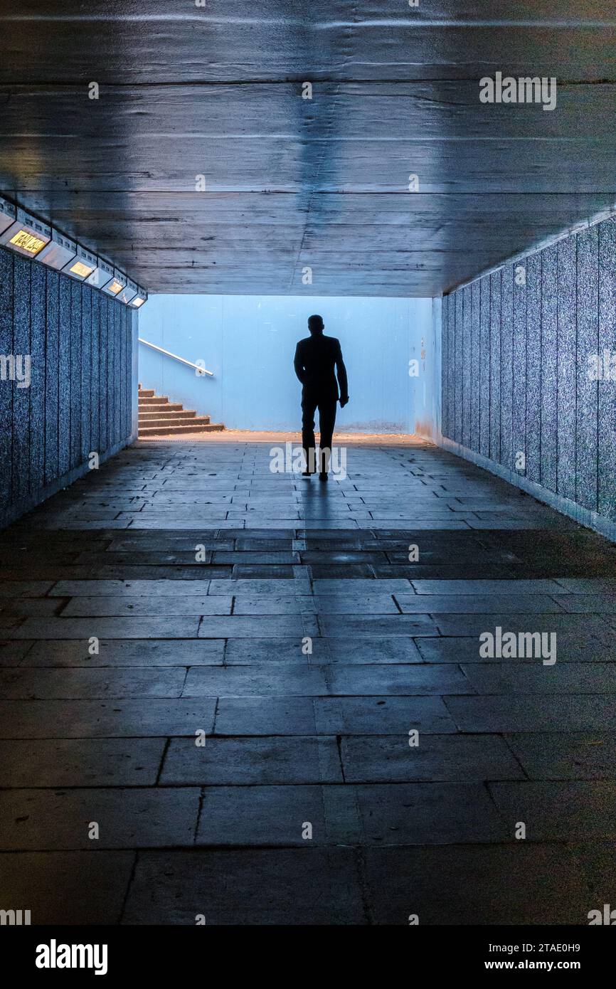 Silhouette of a person walking in a dark pedestrian underpass towards ...