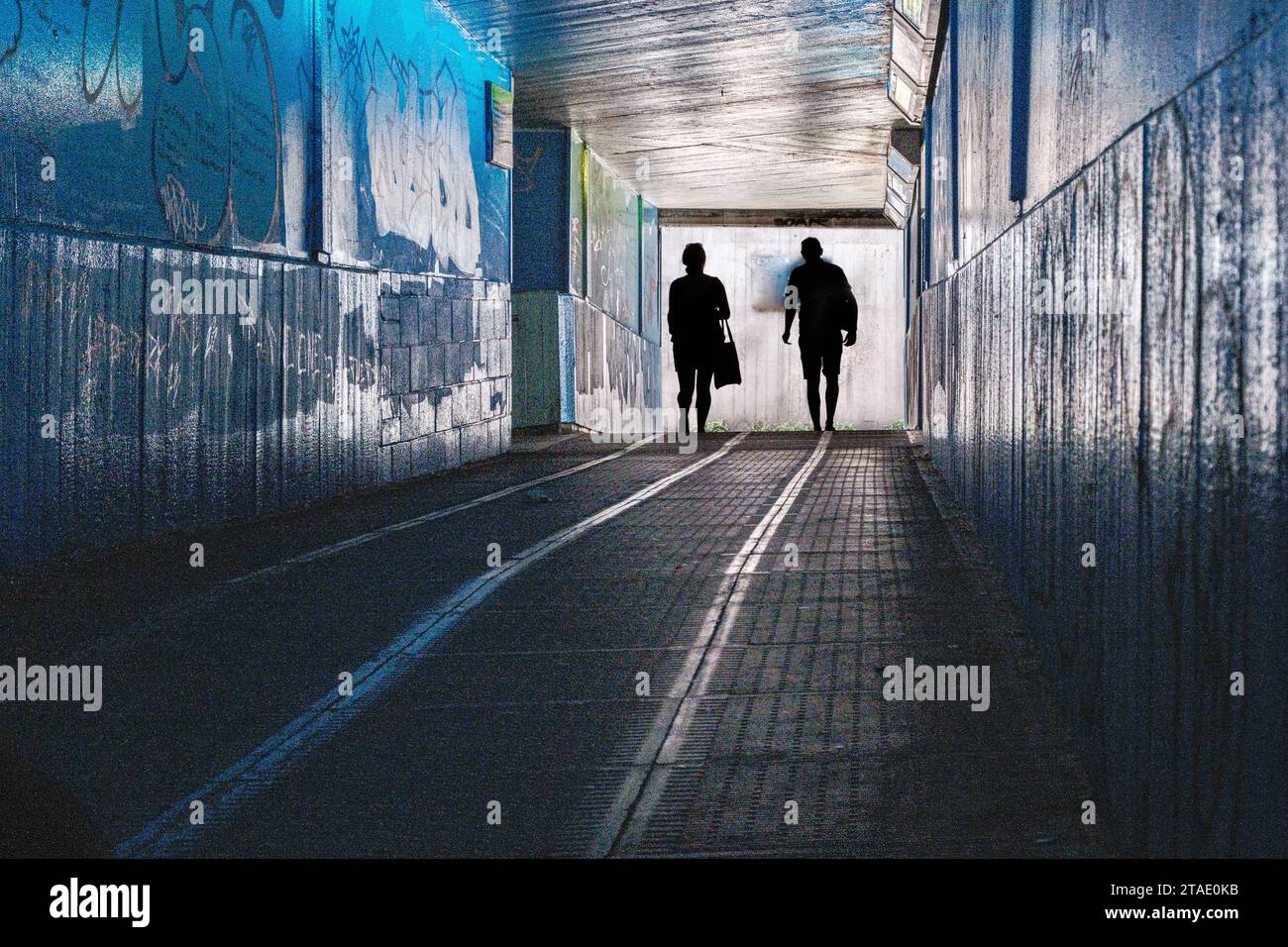 Silhouette of two people walking in a dark pedestrian underpass towards ...