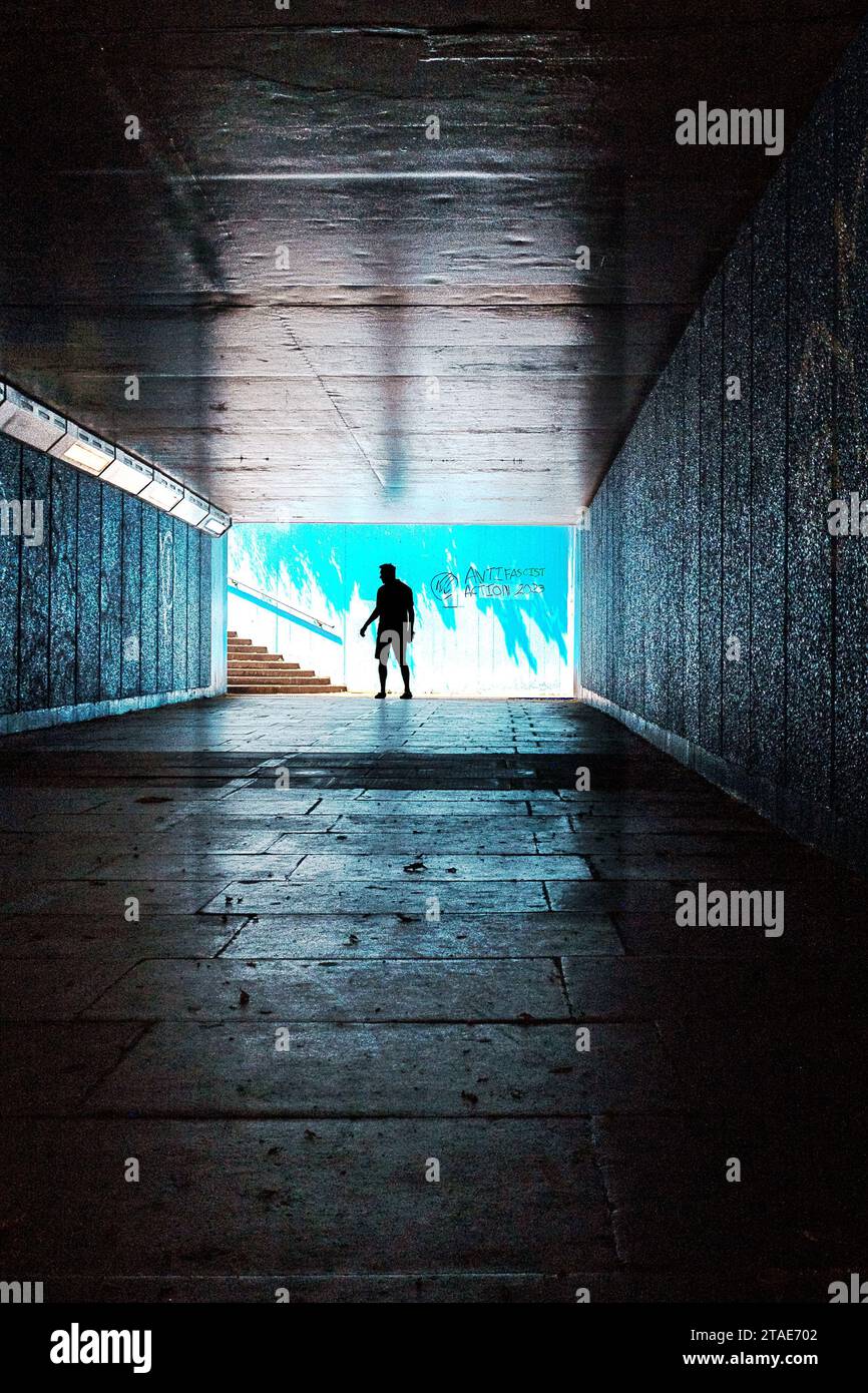 Silhouette of a person walking in a dark pedestrian underpass towards ...