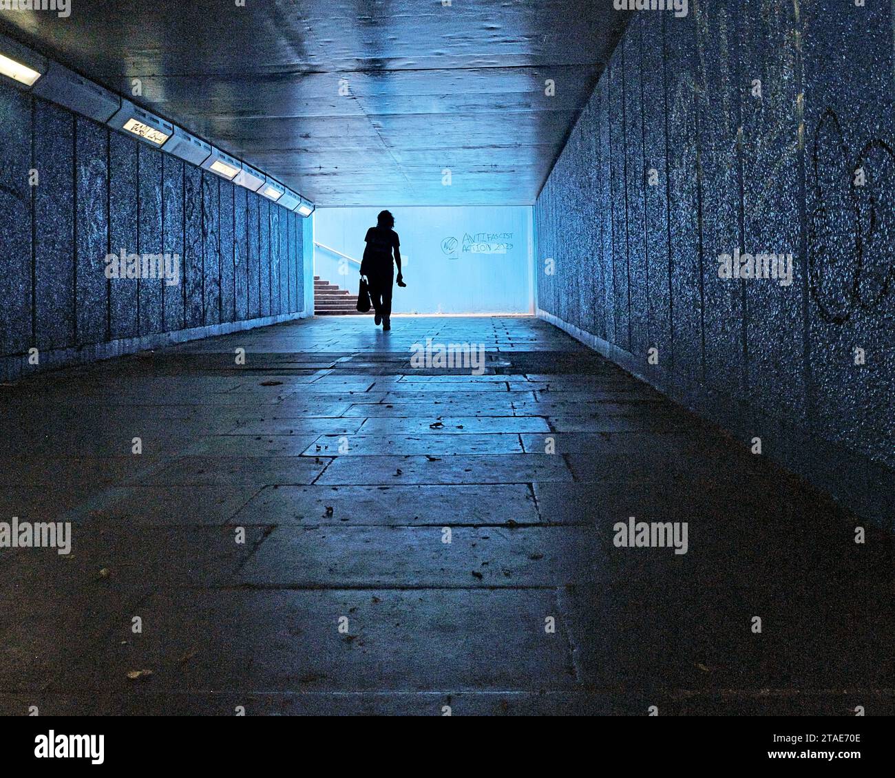 Silhouette of a person walking in a dark pedestrian underpass towards ...