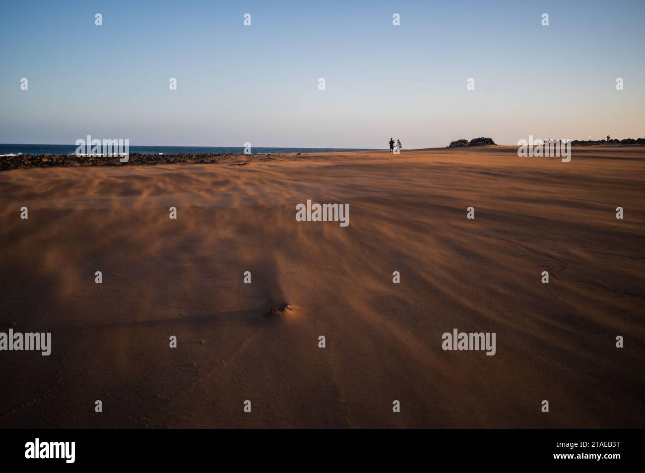Couple walks on the beach as a strong wind blows sand in Lanzarote ...