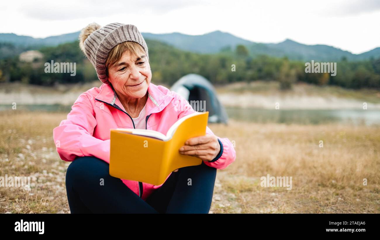 Happy senior woman reading a book outdoors during hiking day. Adventure ...