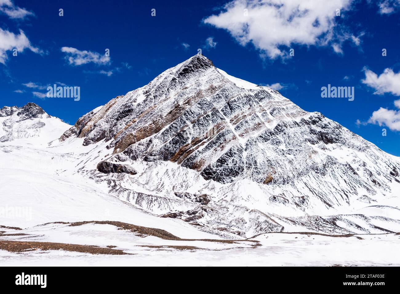 High altitude snowy mountain peak with blue sky and white clouds ...