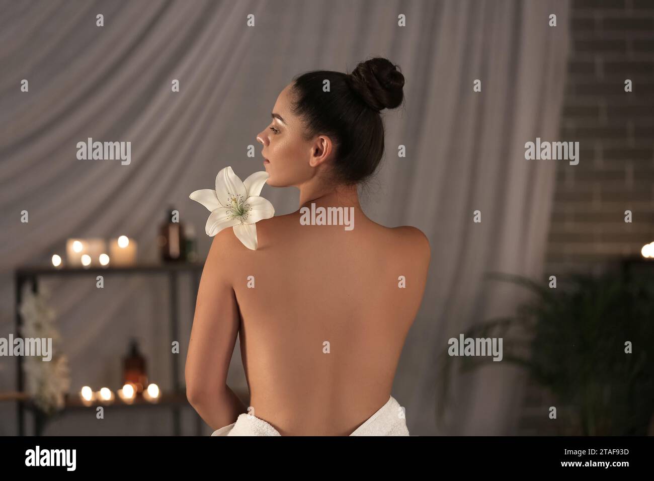 Beautiful young woman with flower relaxing in dark spa salon, back view ...