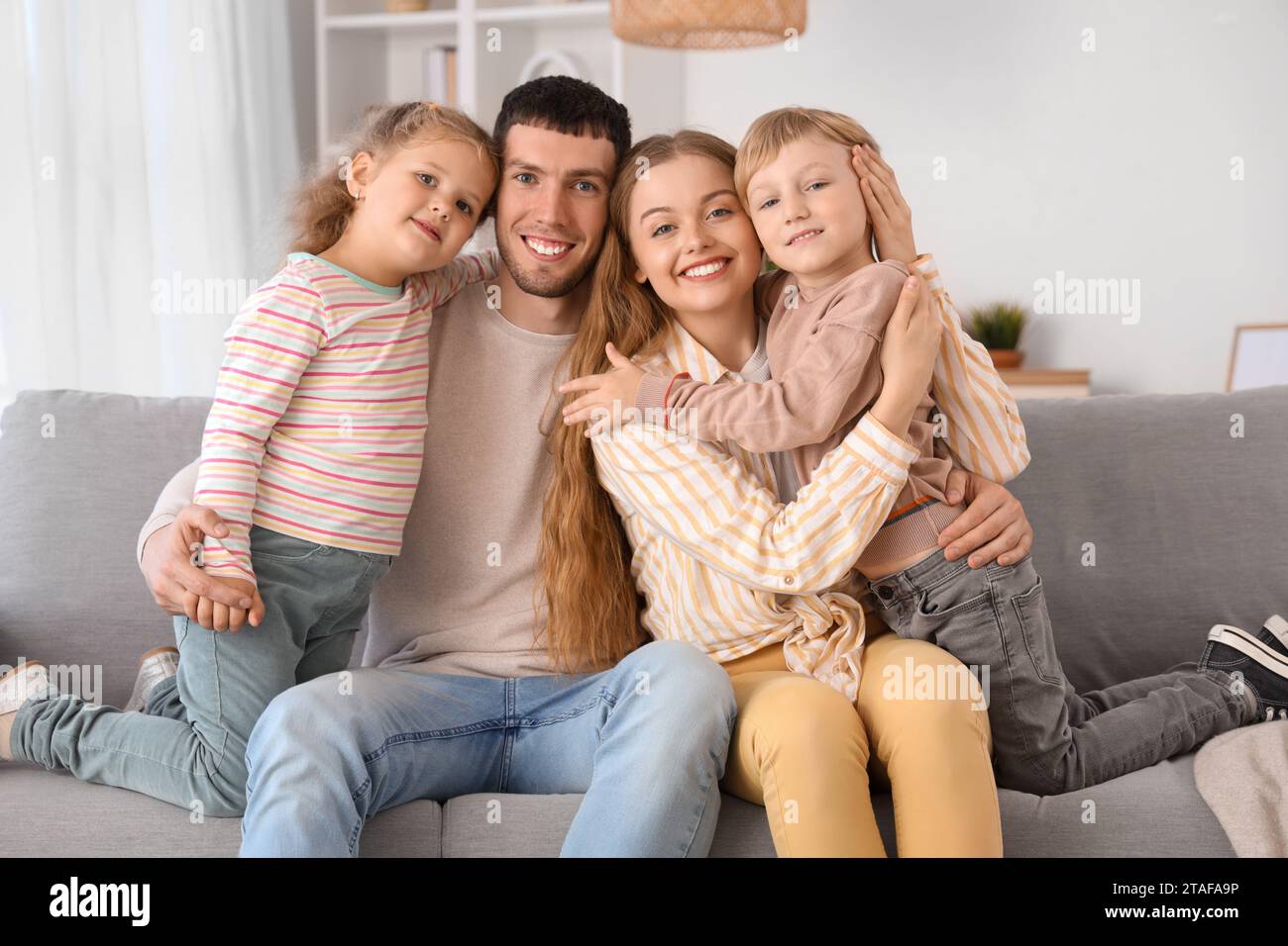 Happy little children with their parents hugging on sofa at home Stock ...