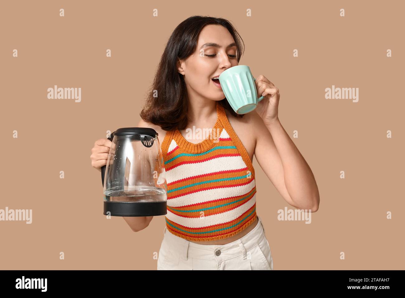 Beautiful young woman with modern electric kettle drinking coffee on ...