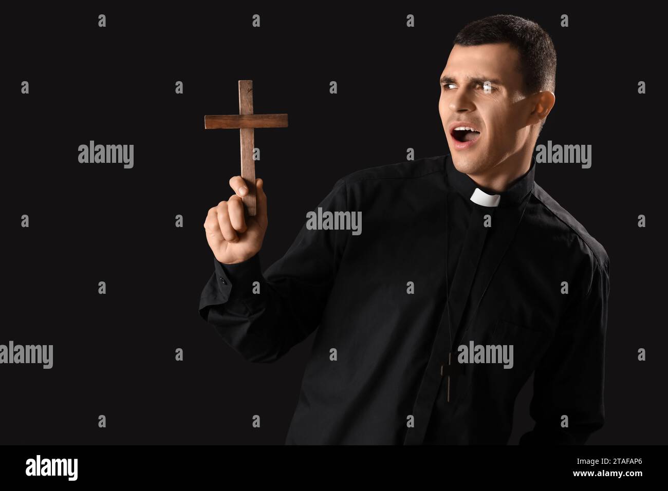 Displeased young priest with cross on dark background Stock Photo - Alamy