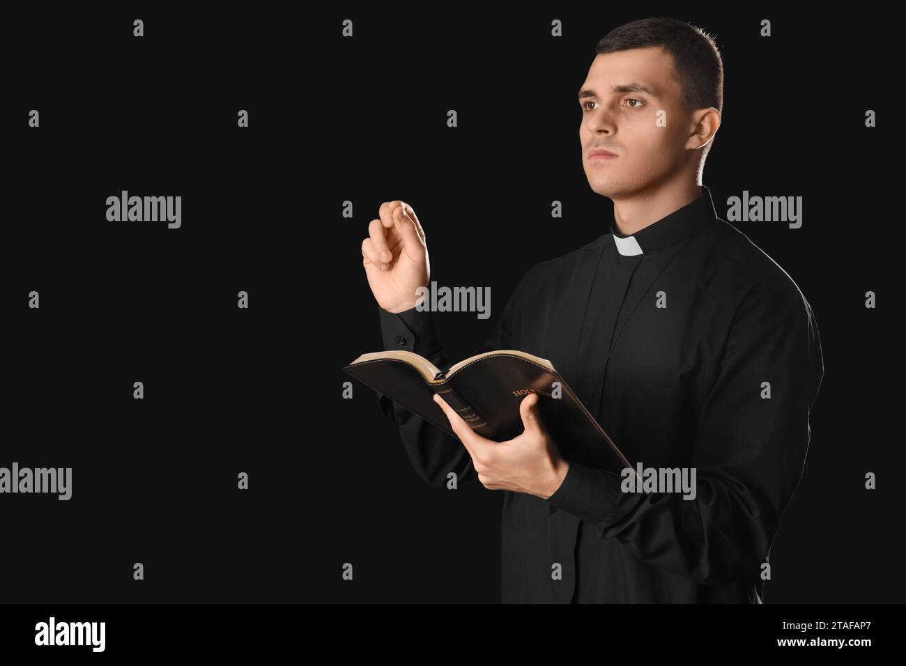 Young priest with Holy Bible on black background Stock Photo - Alamy