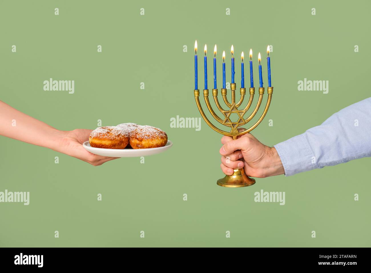 Female and male hands with sufganiyots and Menorah on green background ...