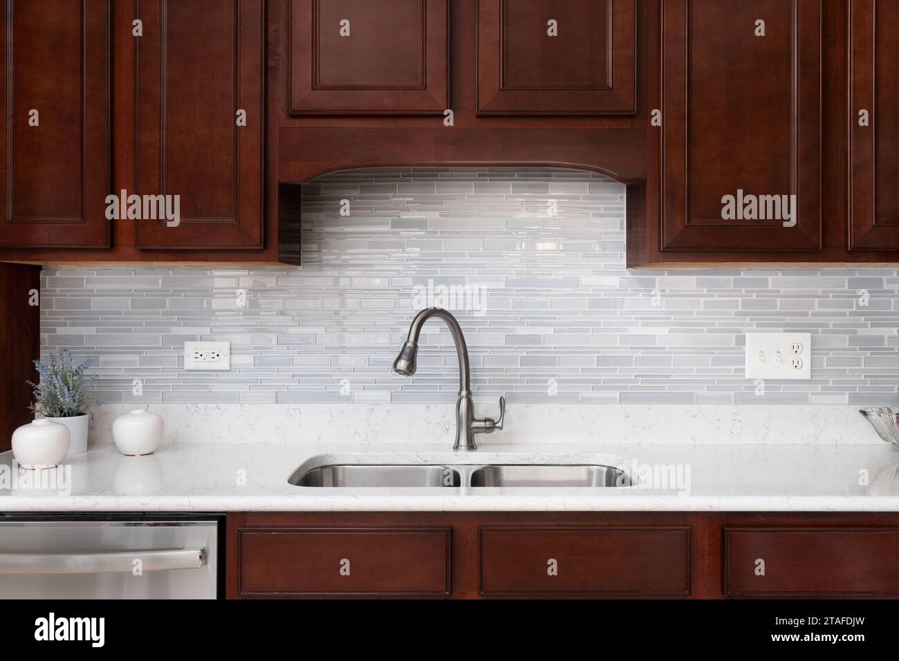 A kitchen faucet detail with a glass tiled backsplash, dark wood ...